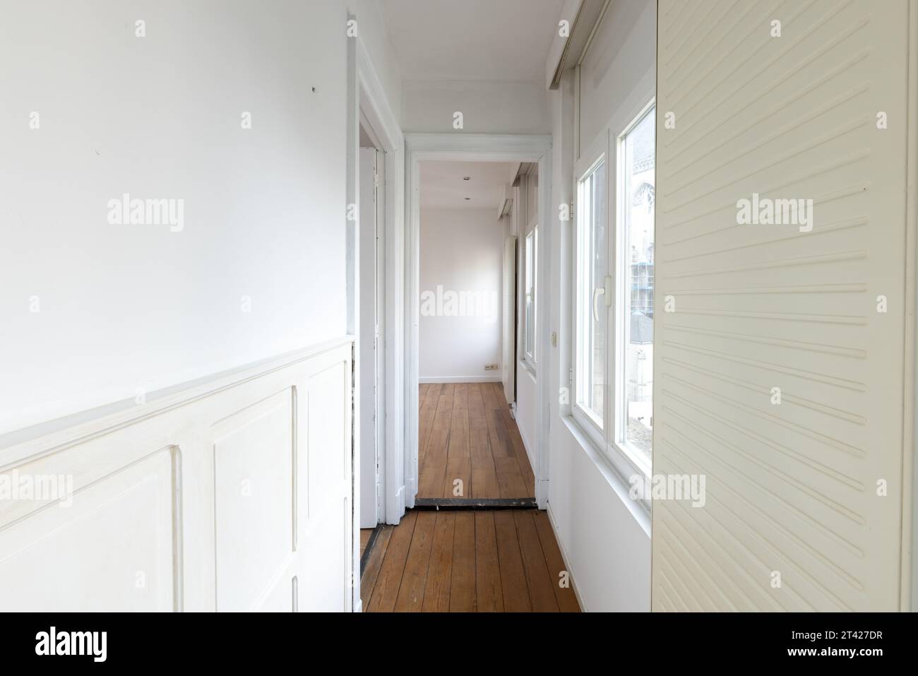 An interior hallway featuring hardwood floors leading to large windows ...