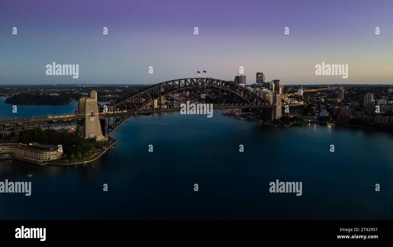 An aerial view of Sydney Harbour Bridge illuminated at dusk from above ...