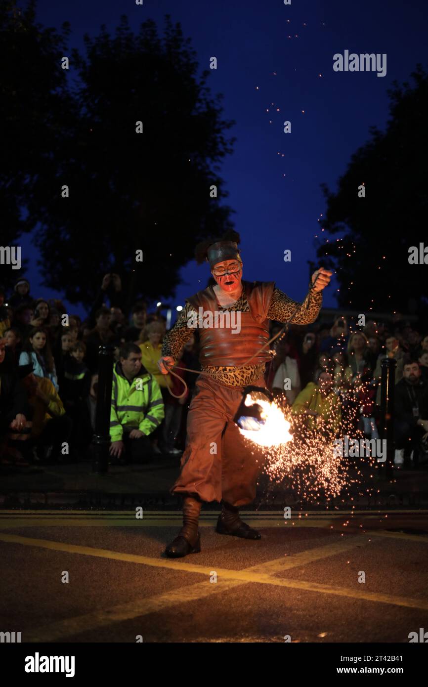 A male wearing a colorful costume and holding a flaming prop performing ...