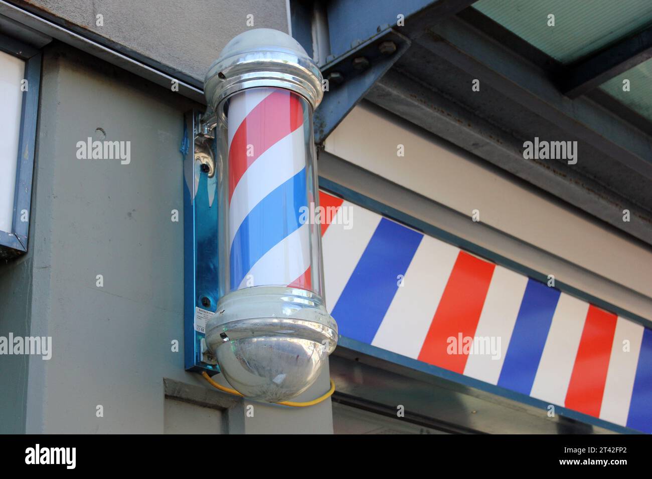 A vibrant red, white and blue barber shop sign hangs outside a ...