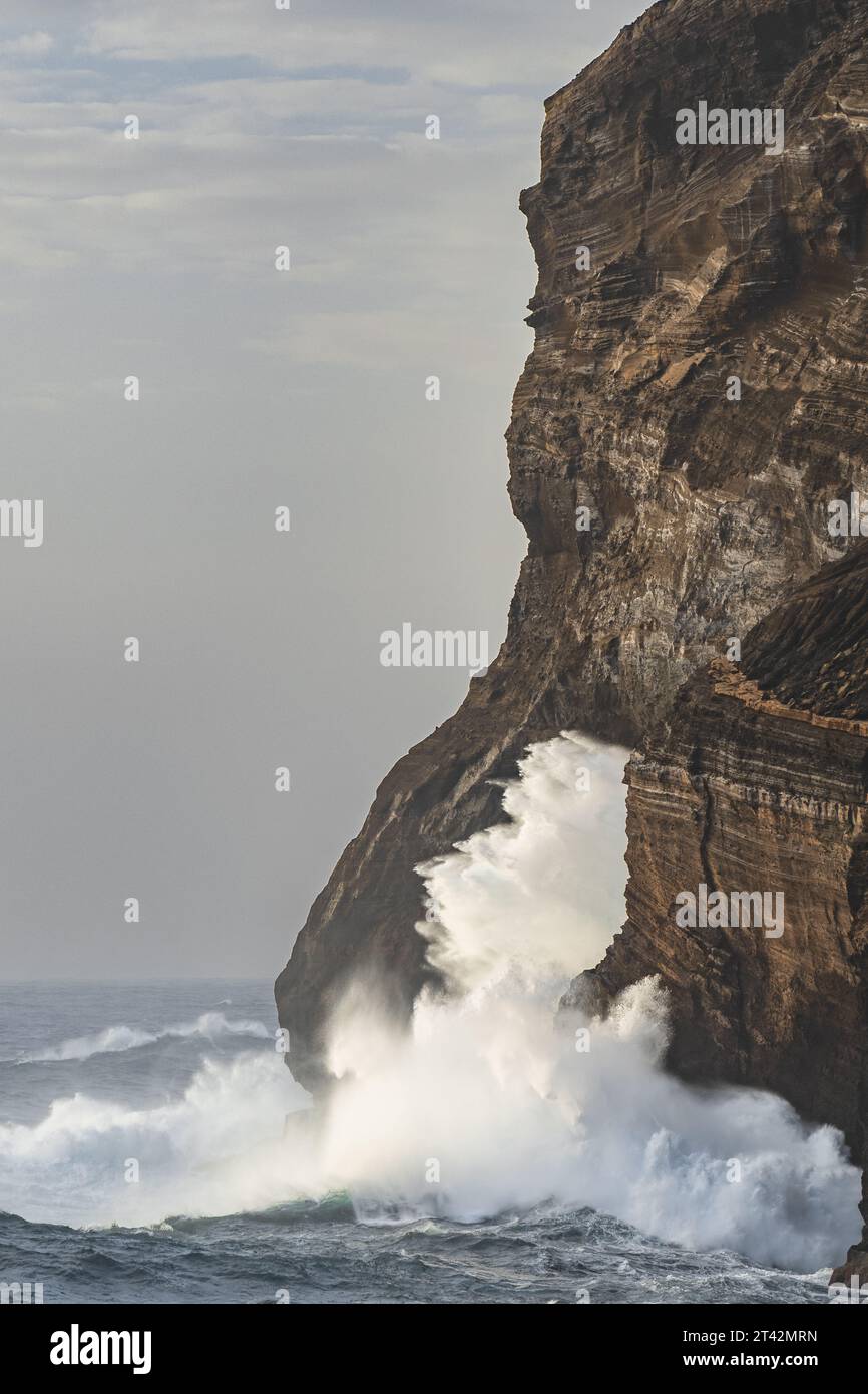 A dramatic scene of powerful waves crashing against a rocky shoreline ...