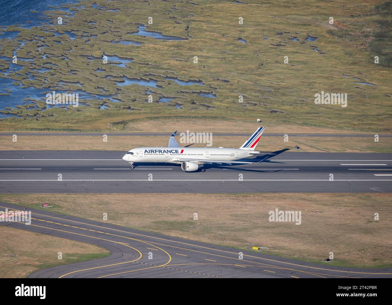 A commercial aircraft parked atop a sunlit tarmac of an airport runway ...