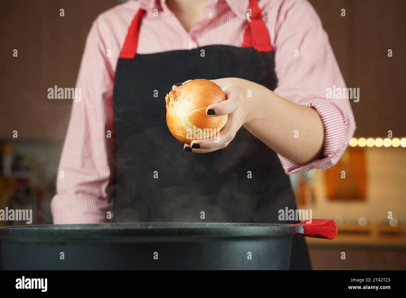 Woman adding onion with skins at chicken soup, chicken broth, in a pot ...