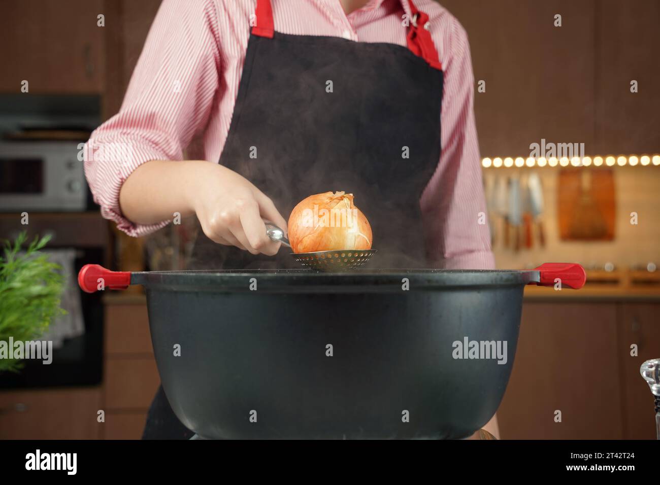 Woman adding onion with skins at chicken soup, chicken broth, in a pot ...