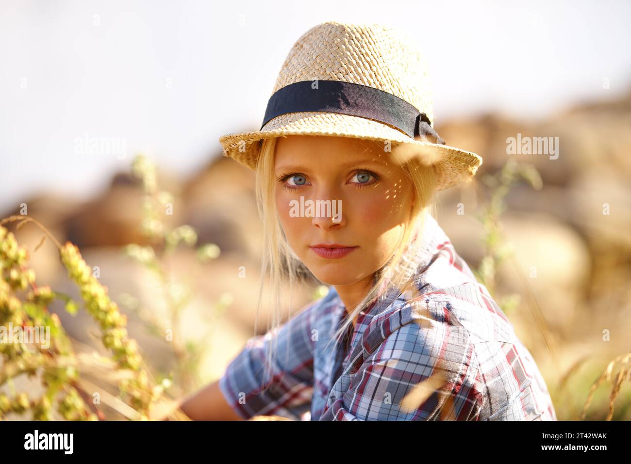 Serious, portrait and young woman in nature with straw hat sitting in ...