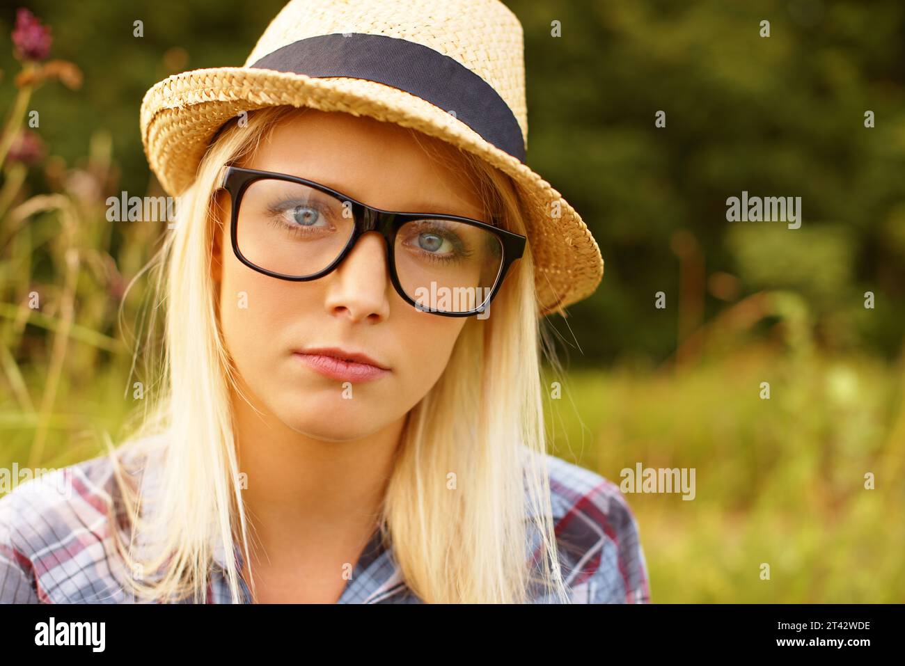 Glasses, portrait and young woman in nature with a straw hat sitting in ...