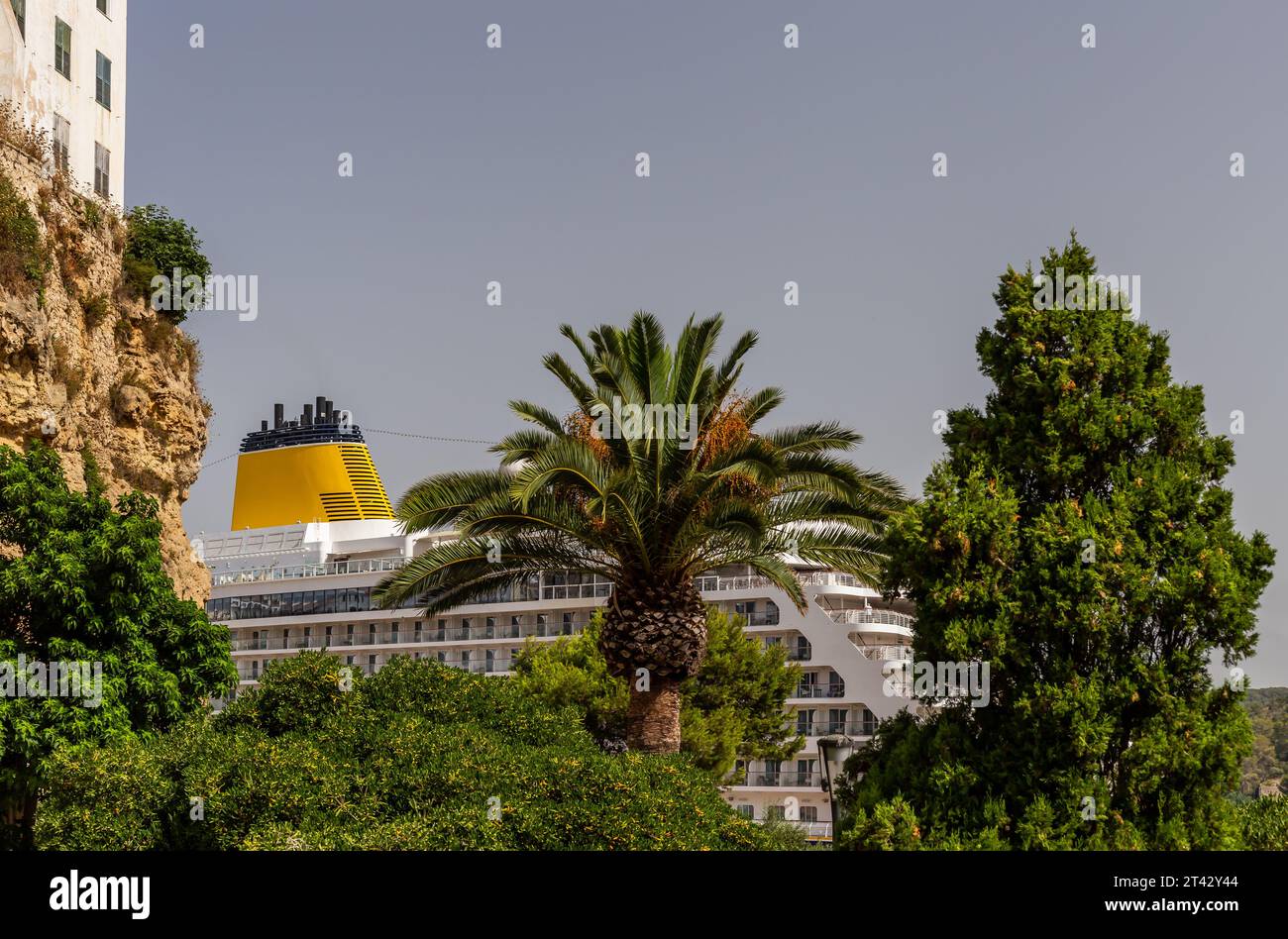 A very large cruise ship docks in Mahon in Minorca.Palm trees adds to ...
