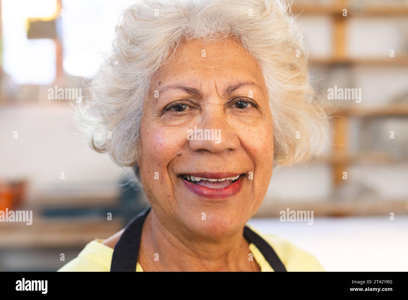 Happy biracial senior female potter with gray hair, looking on camera ...