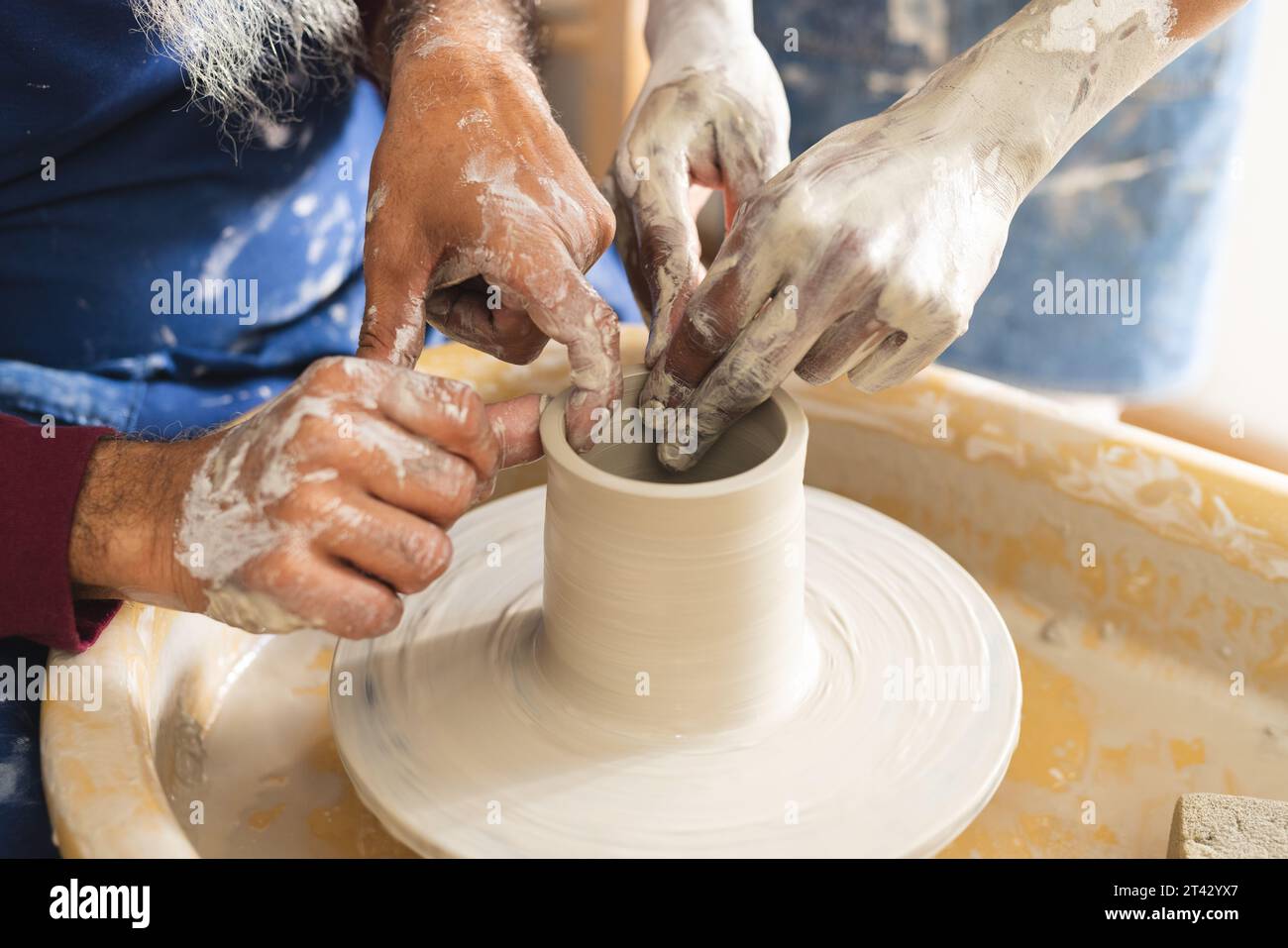 Hands of two diverse male potters working on clay vase using potter's ...