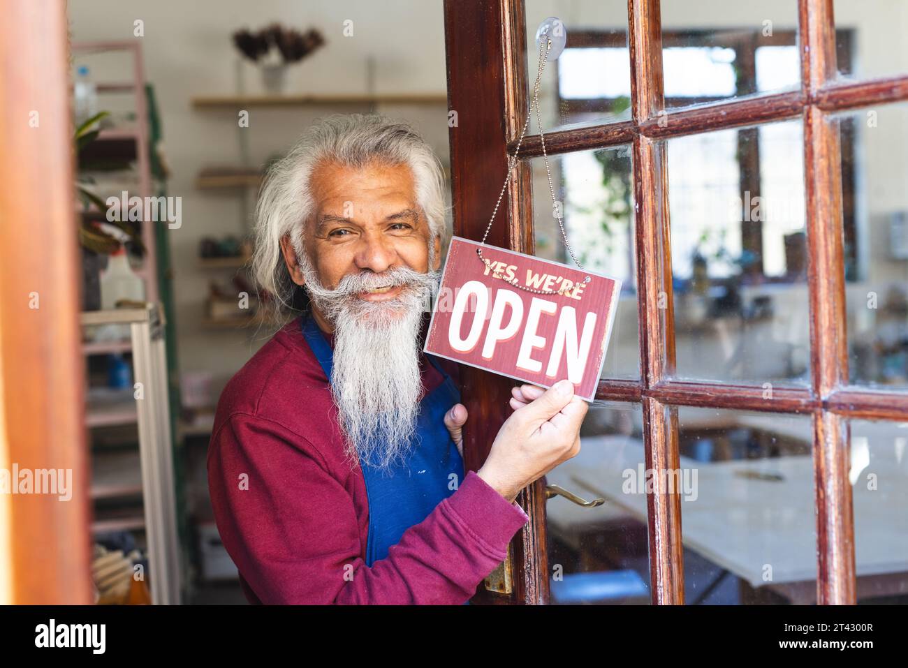 Happy biracial senior business owner with long beard, changing shop ...