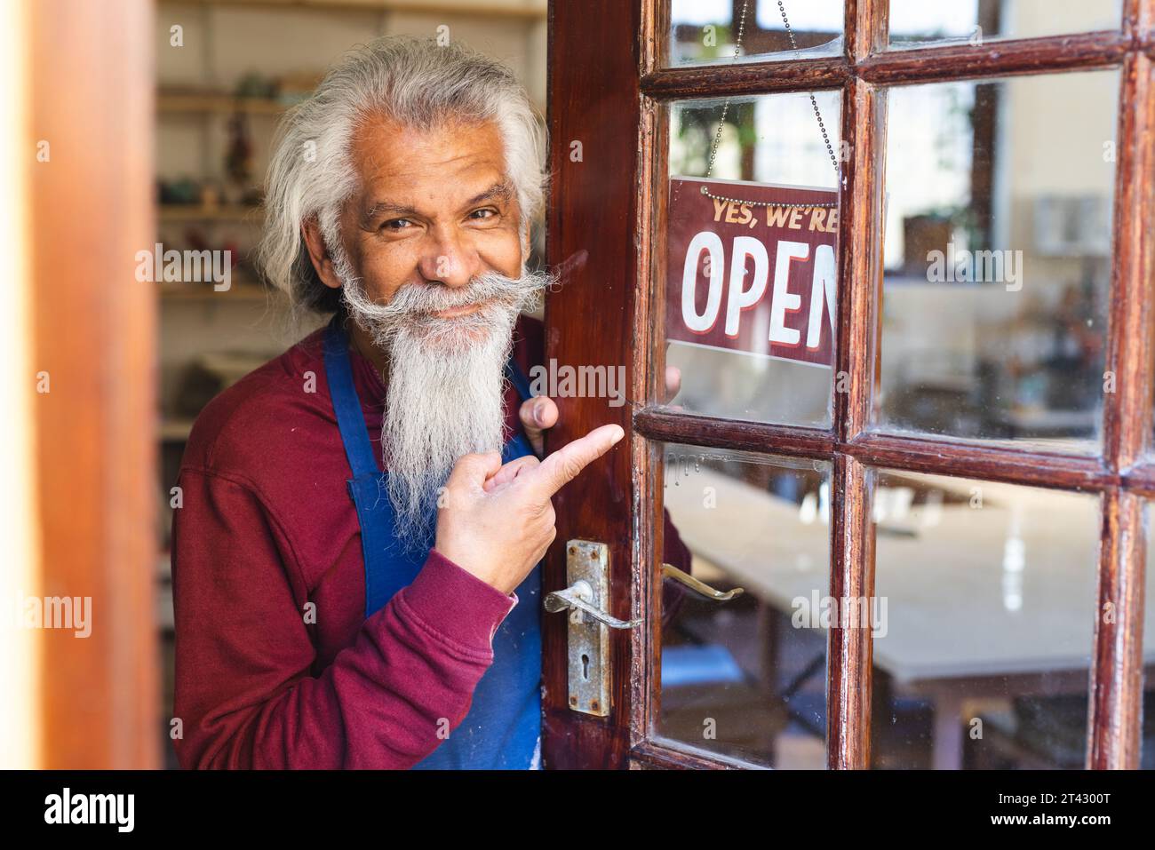 Happy biracial senior business owner with long beard showing shop sign ...