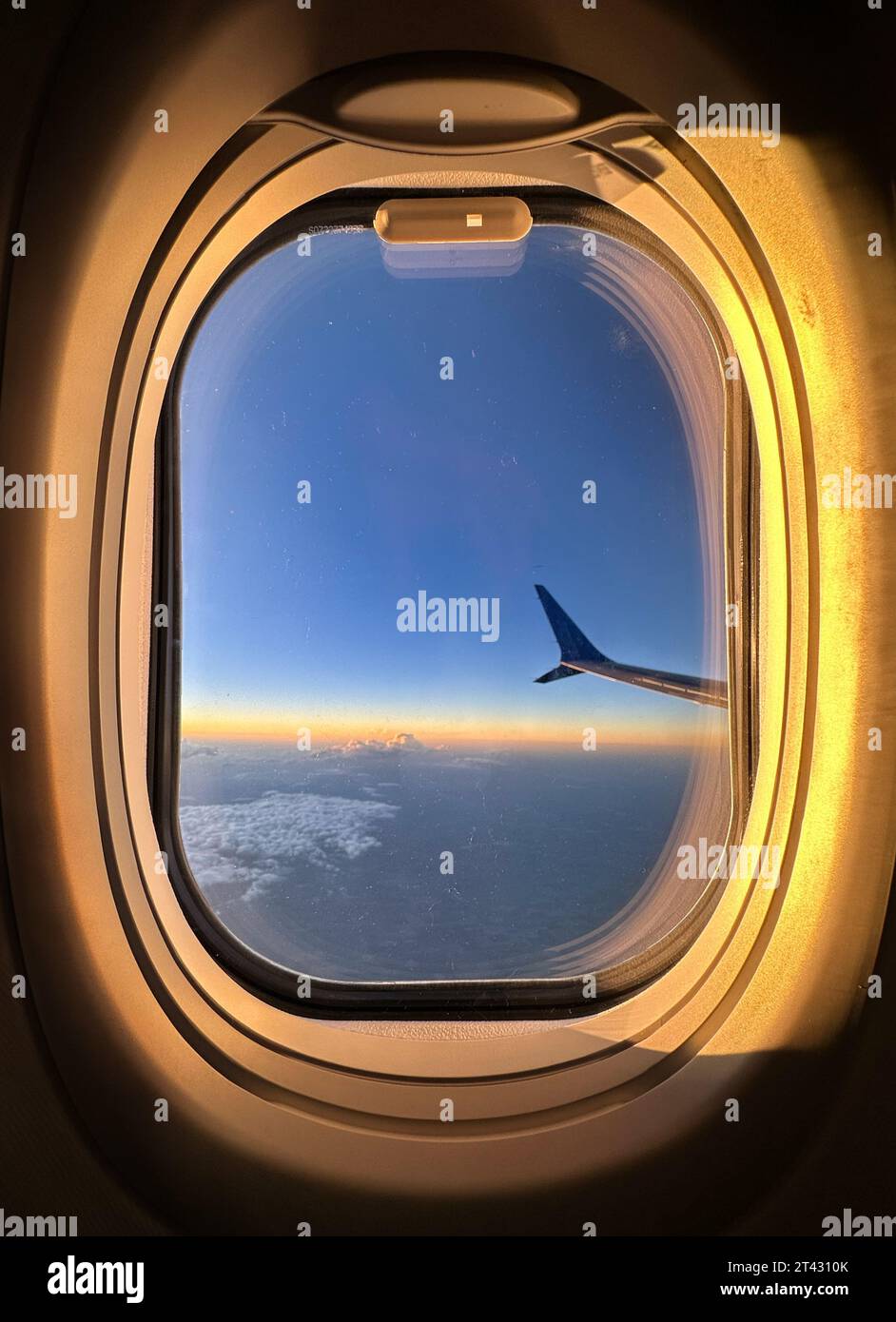 Aircraft wing and sunset skyscape through a plane window in flight ...