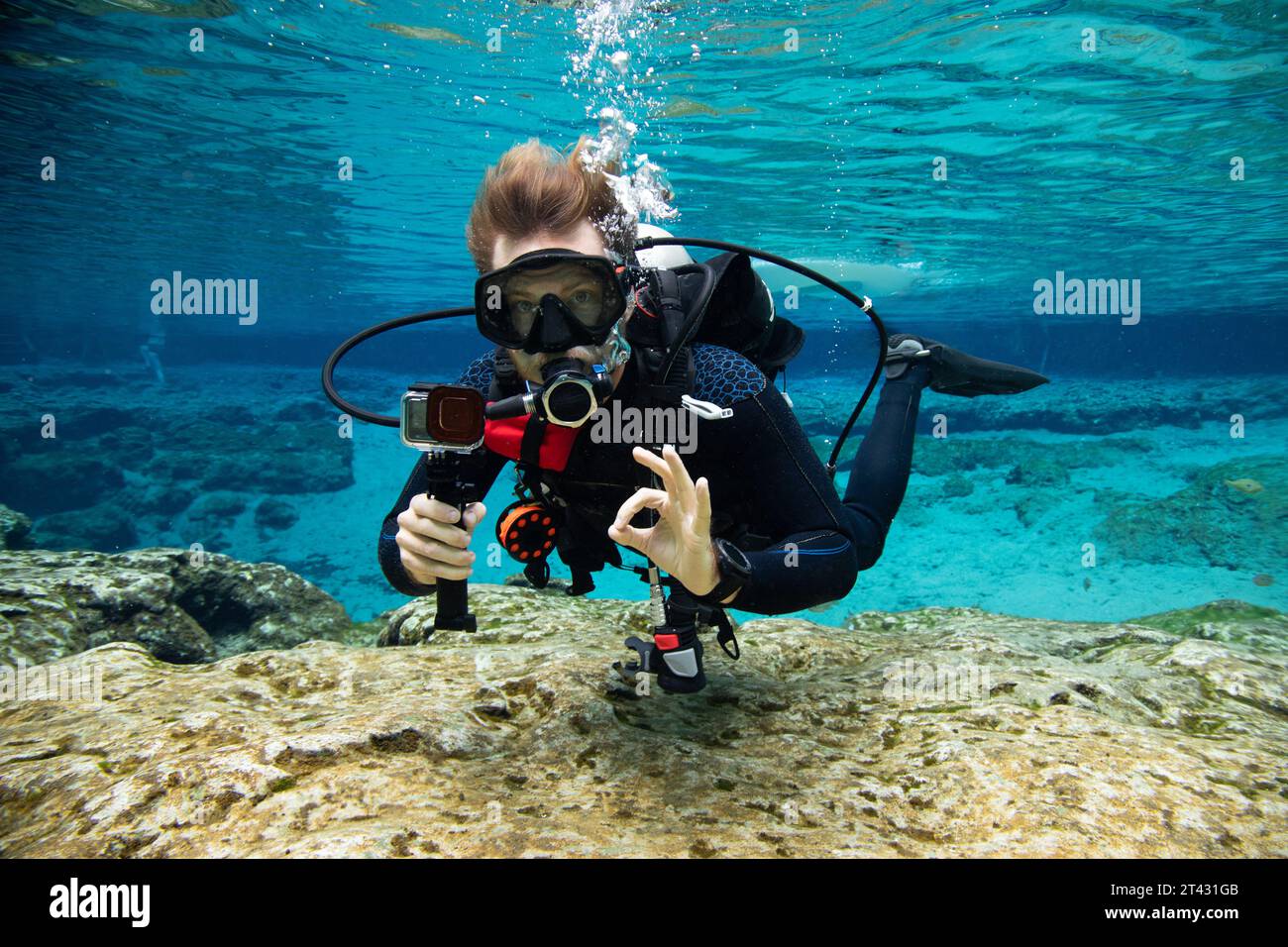 Underwater portrait of a scuba diver swimming near seabed making an ok ...