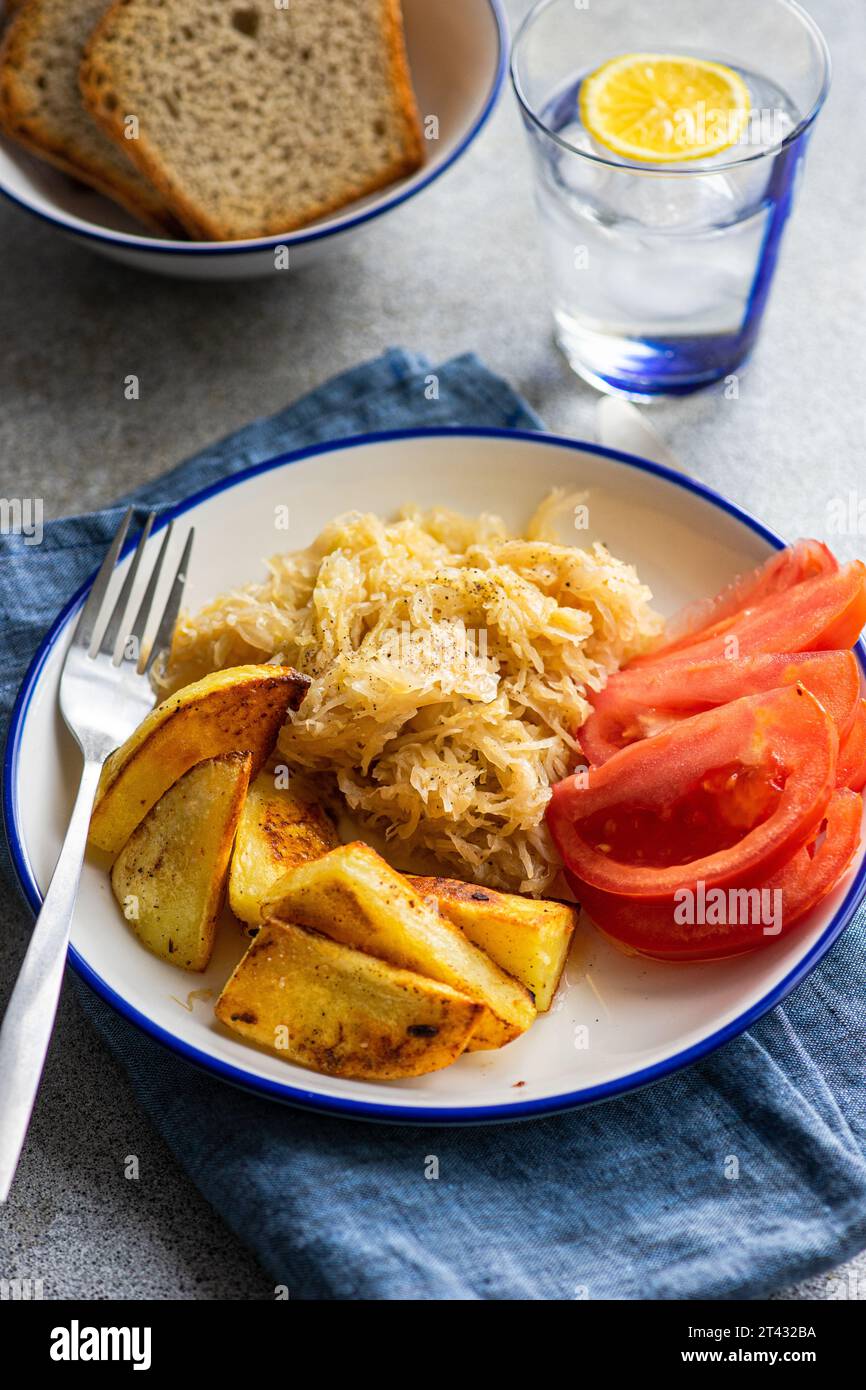 Fermented cabbage salad with baked potato, tomato, bread and a glass of ...