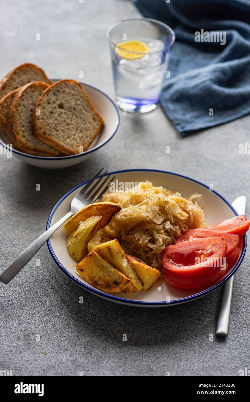 Fermented cabbage salad with baked potato, tomato, bread and a glass of ...