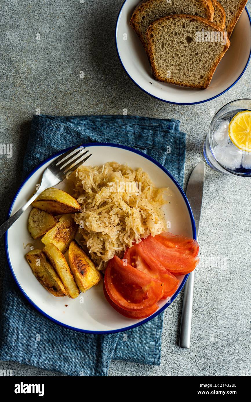 Overhead view of a fermented cabbage salad with baked potato, tomato ...