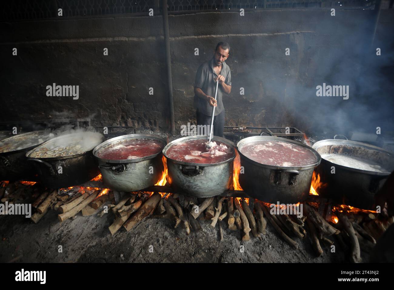 Palestinian men prepare food in large pots simmering on wooden fires ...