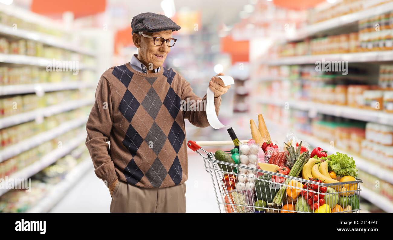 Elderly male customer with a shopping cart looking at a bill inside a ...