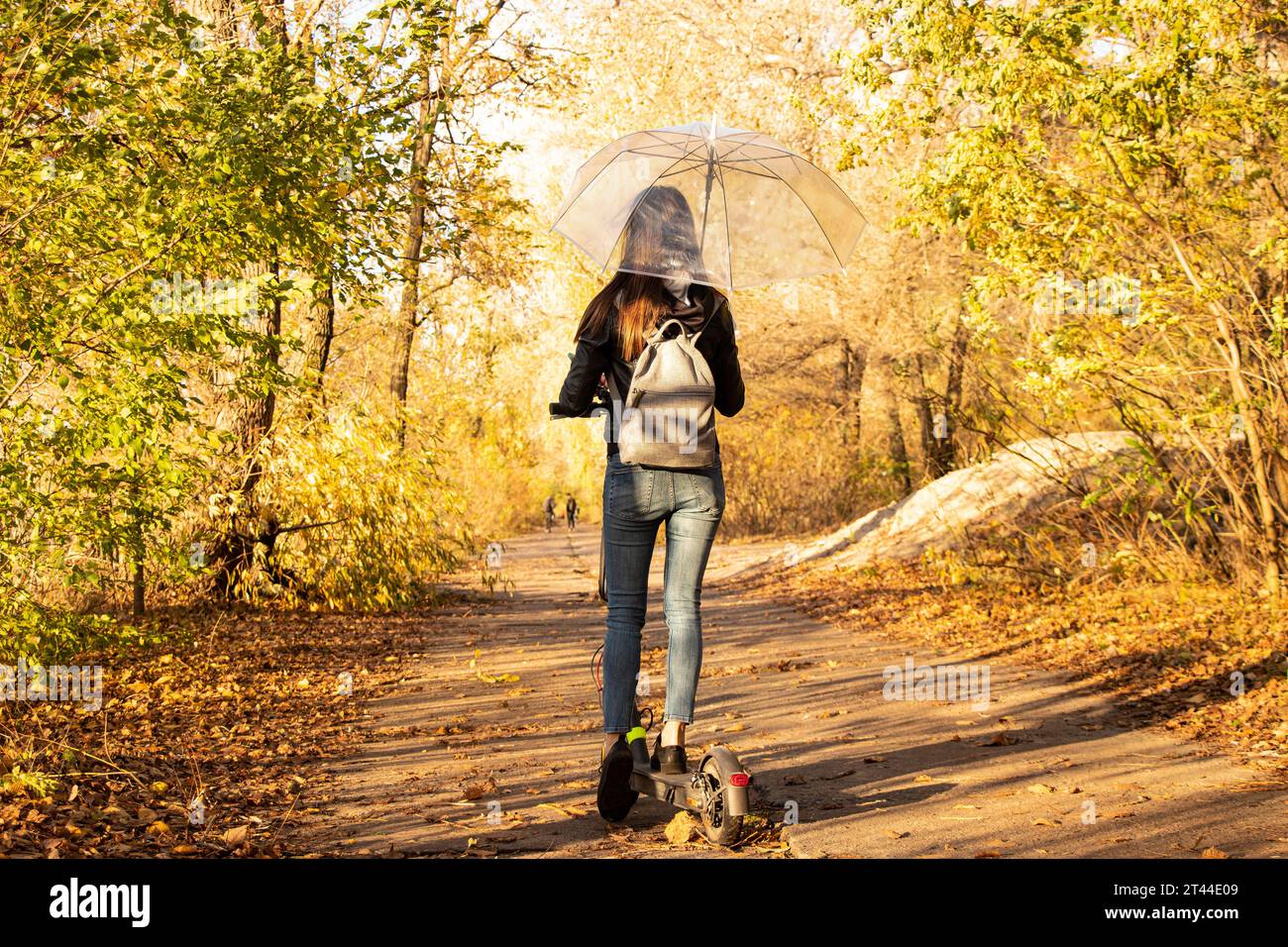 A girl on an electric scooter in the fall under a transparent umbrella ...