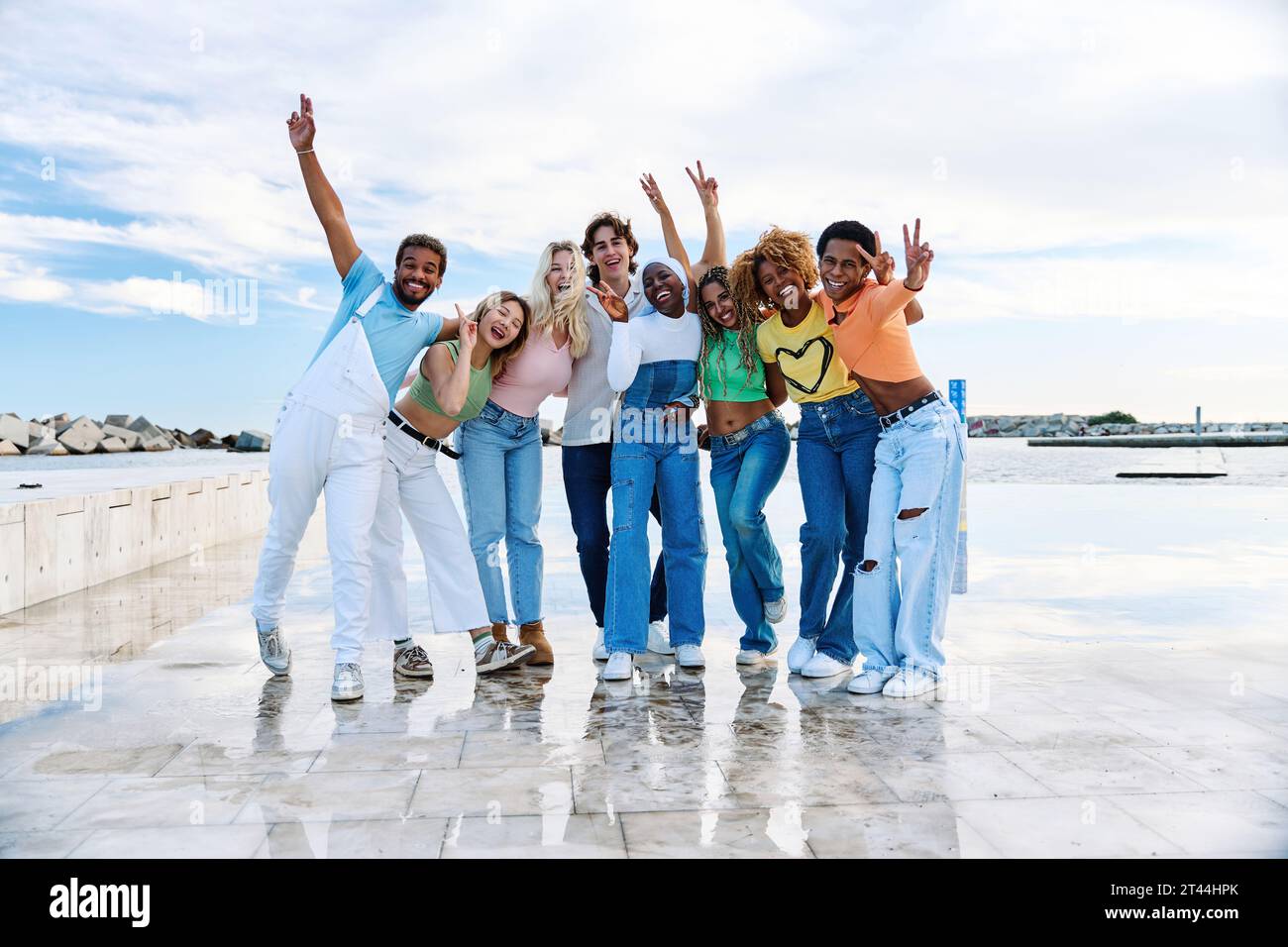 Happy multi-ethnic friends raising hands and gesturing peace outdoors ...