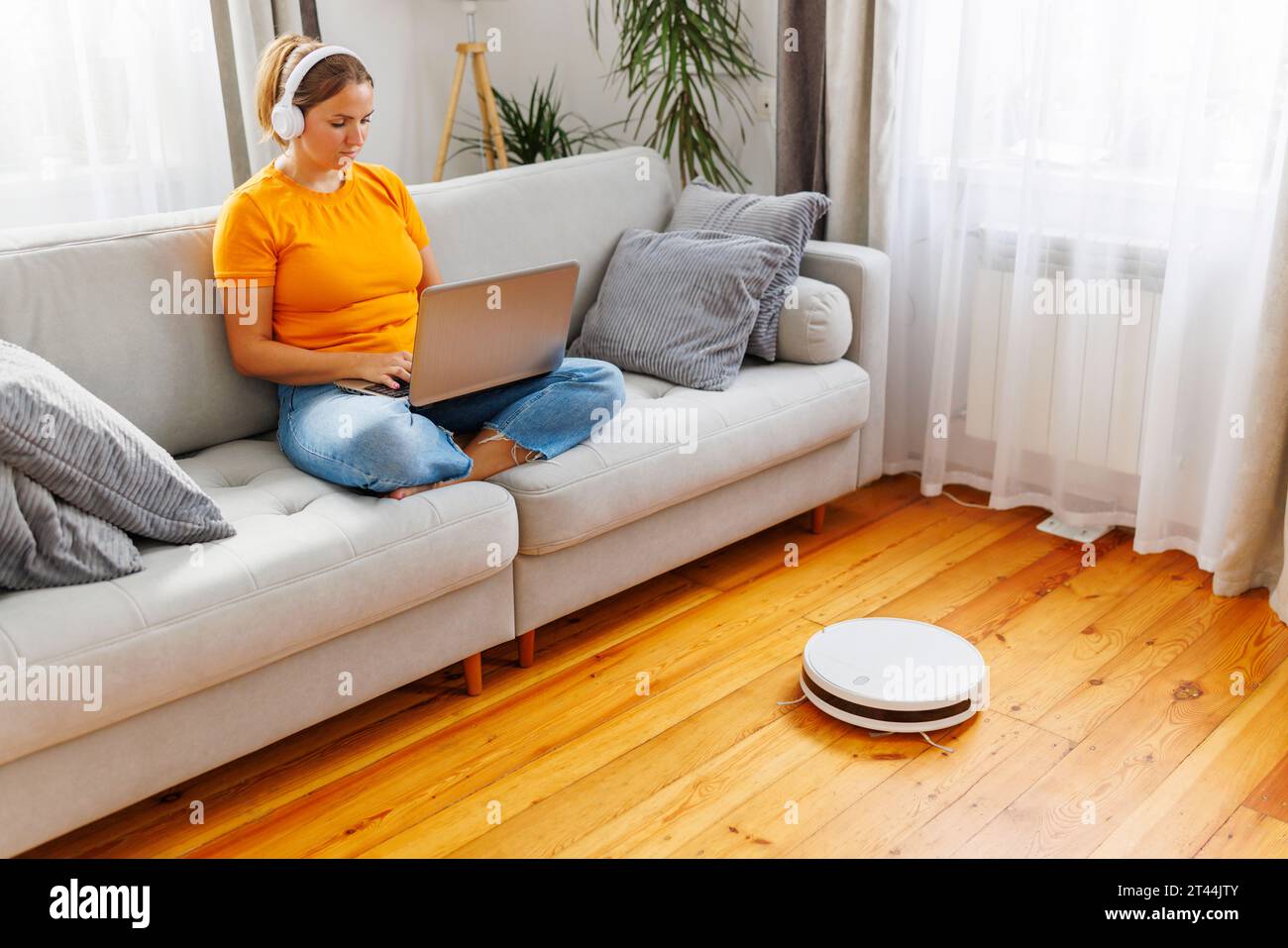 Robotic vacuum cleaner cleaning room while woman resting on sofa using ...