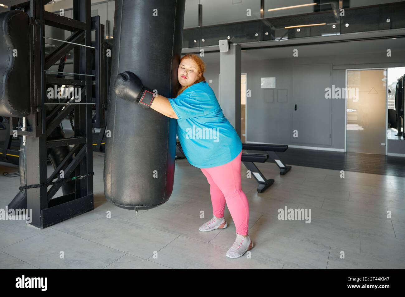 Tired exhausted fat woman leaning and hugging punching bag while ...