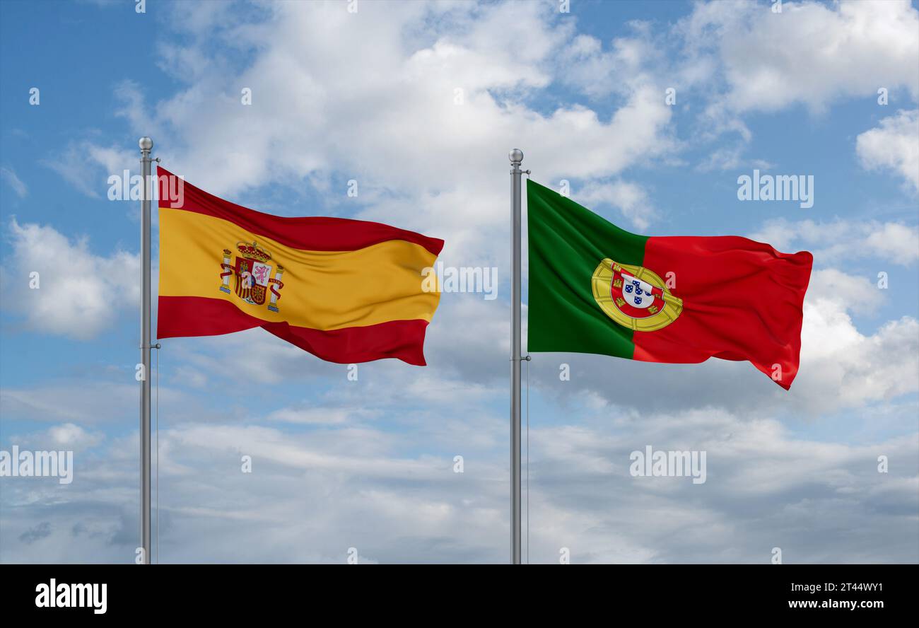 Portugal and Spain flags waving together in the wind on blue cloudy sky ...