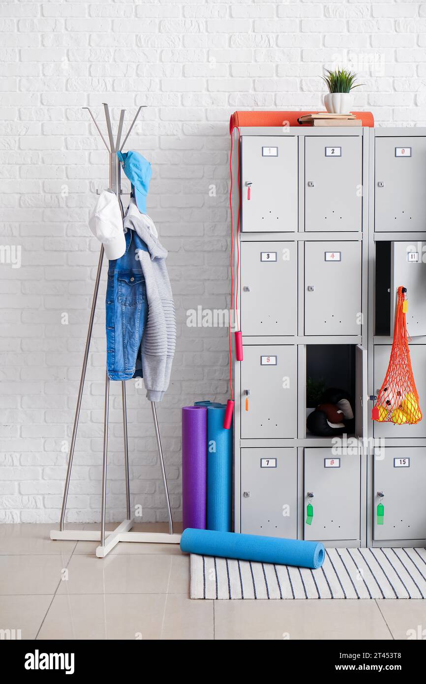 Modern locker with sports equipment and rack near white brick wall ...