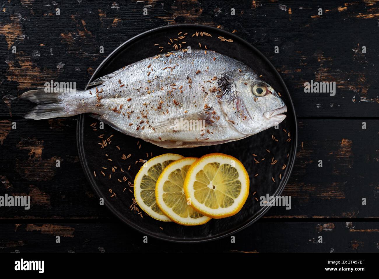 Raw dorado fish with lemon and cumin seeds on black plate. Top view ...