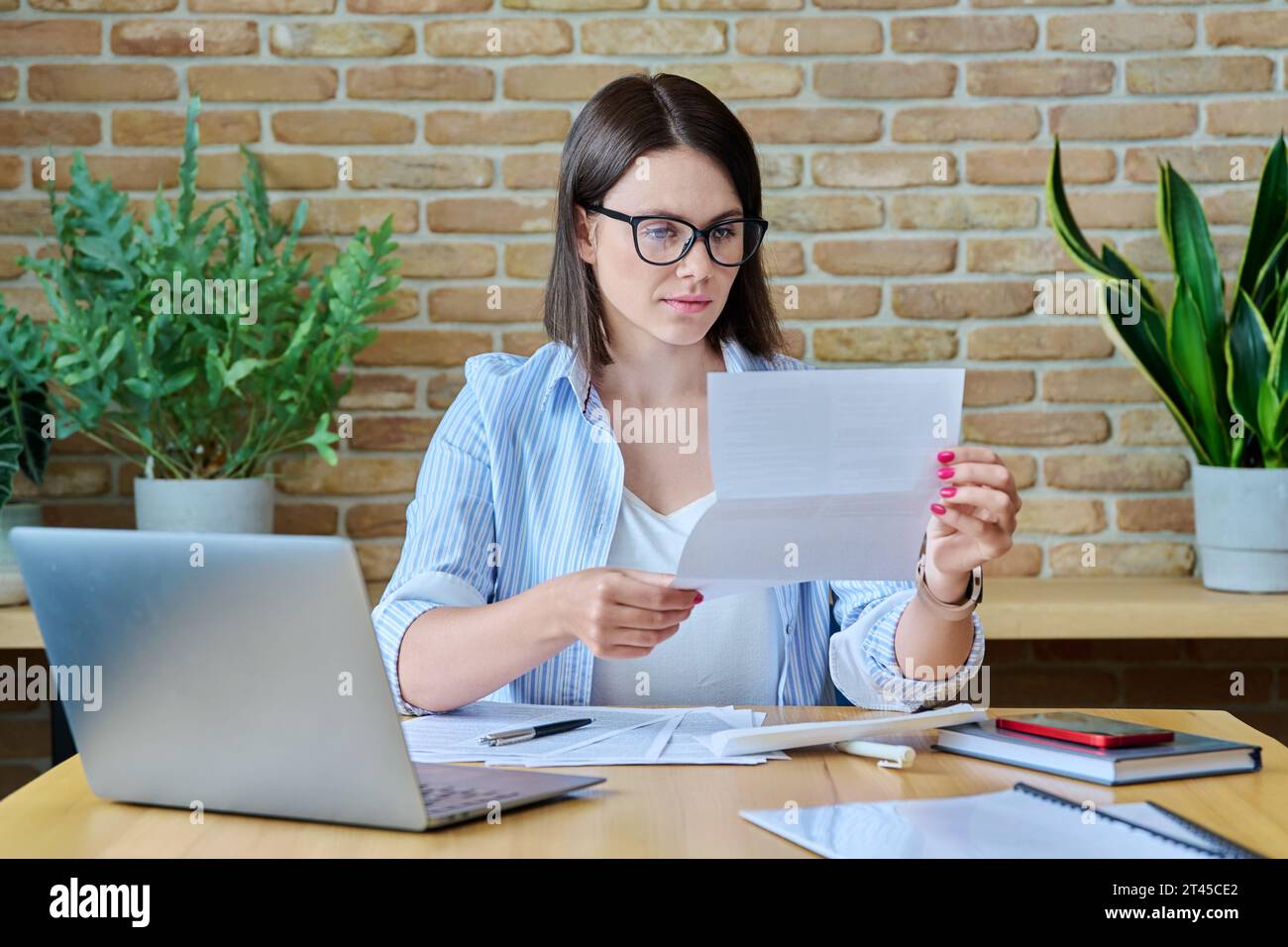 Serious young business woman reading official letter, sitting in office ...