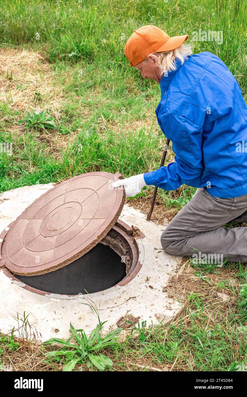 A plumber opens a manhole cover on a concrete well. Inspection and ...