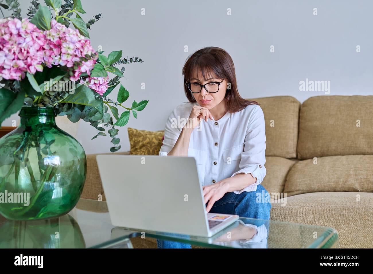 Serious middle aged woman working with laptop computer, in home office ...