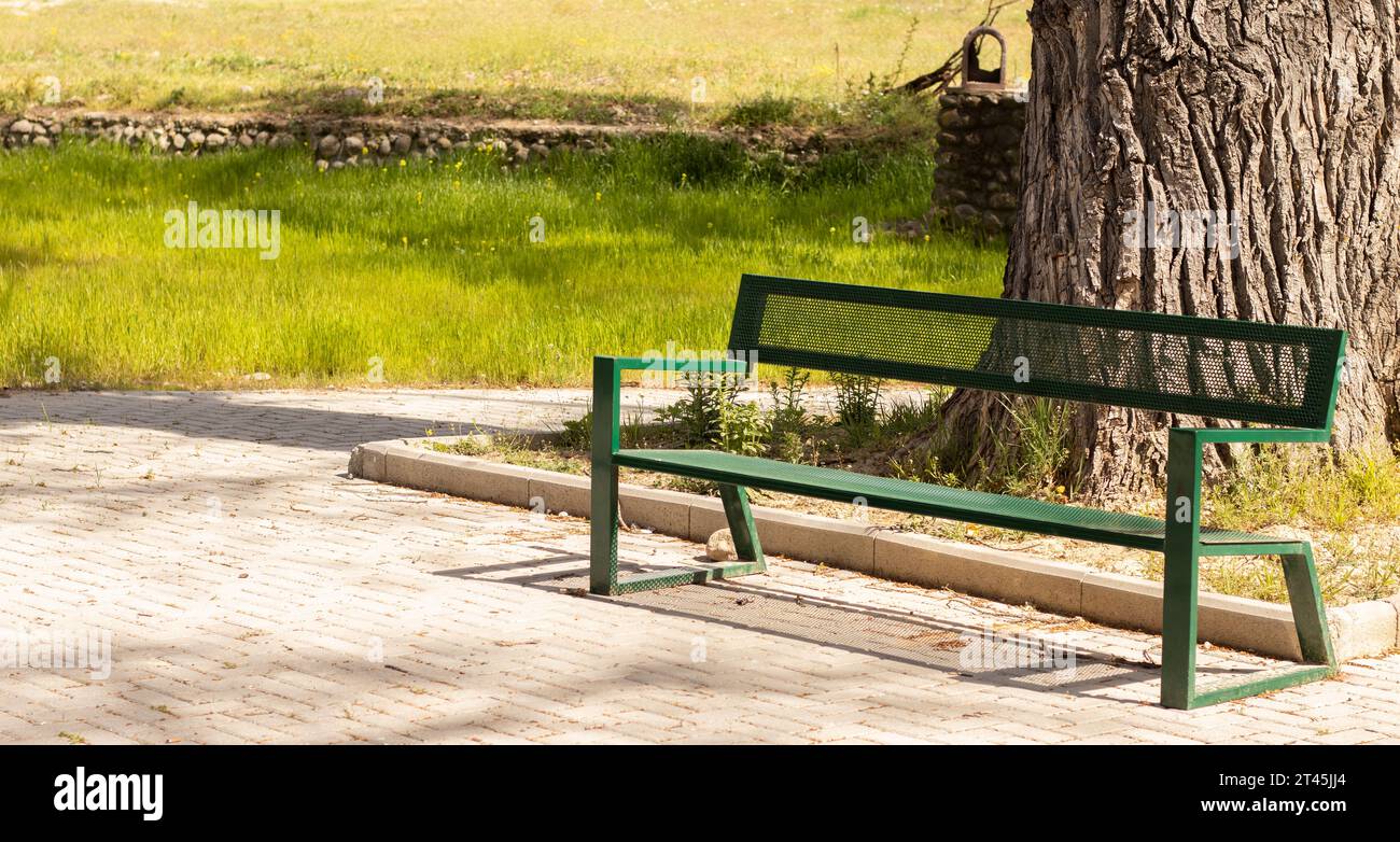 Green metal bench in the park during the midday sun in springtime ...