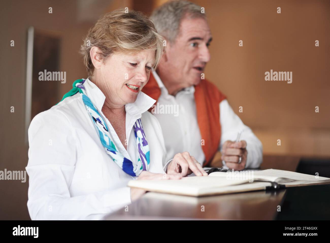 Senior couple, reading and signing documents at hotel reception desk ...