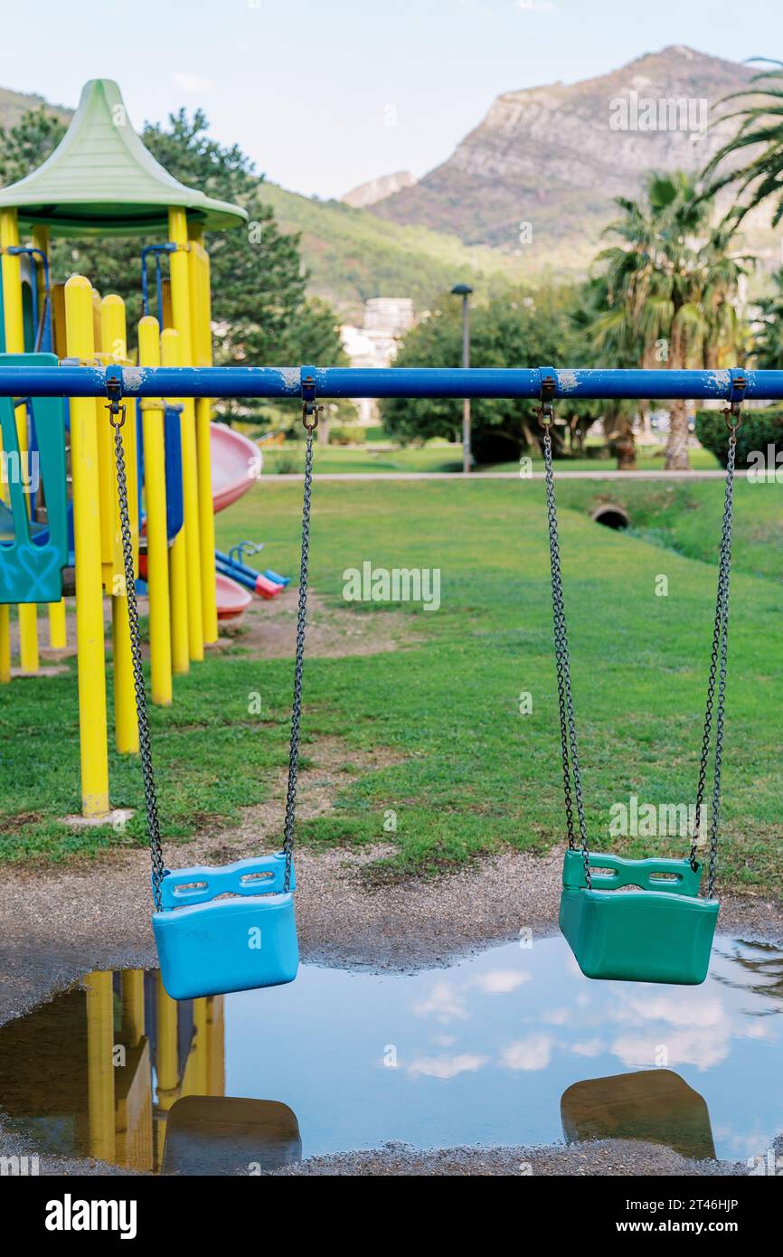 Plastic chain swings in the playground hanging over puddles after rain ...
