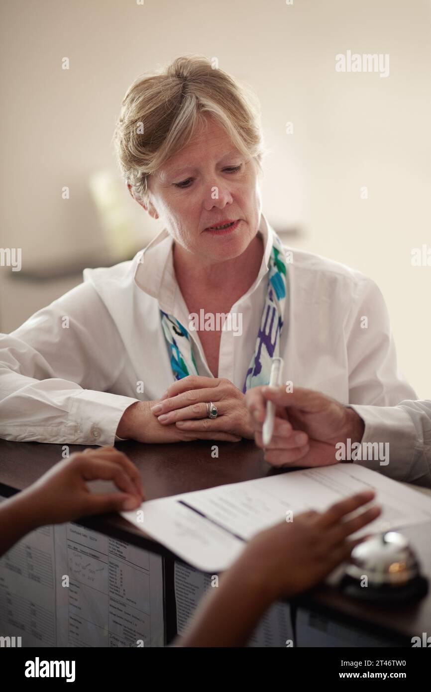 Senior woman, hotel and signing documents at reception desk for booking ...