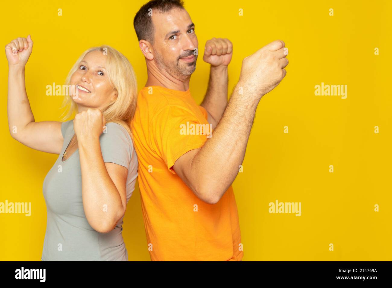 Back to back happy caucasian couple in their 40s celebrating victory ...