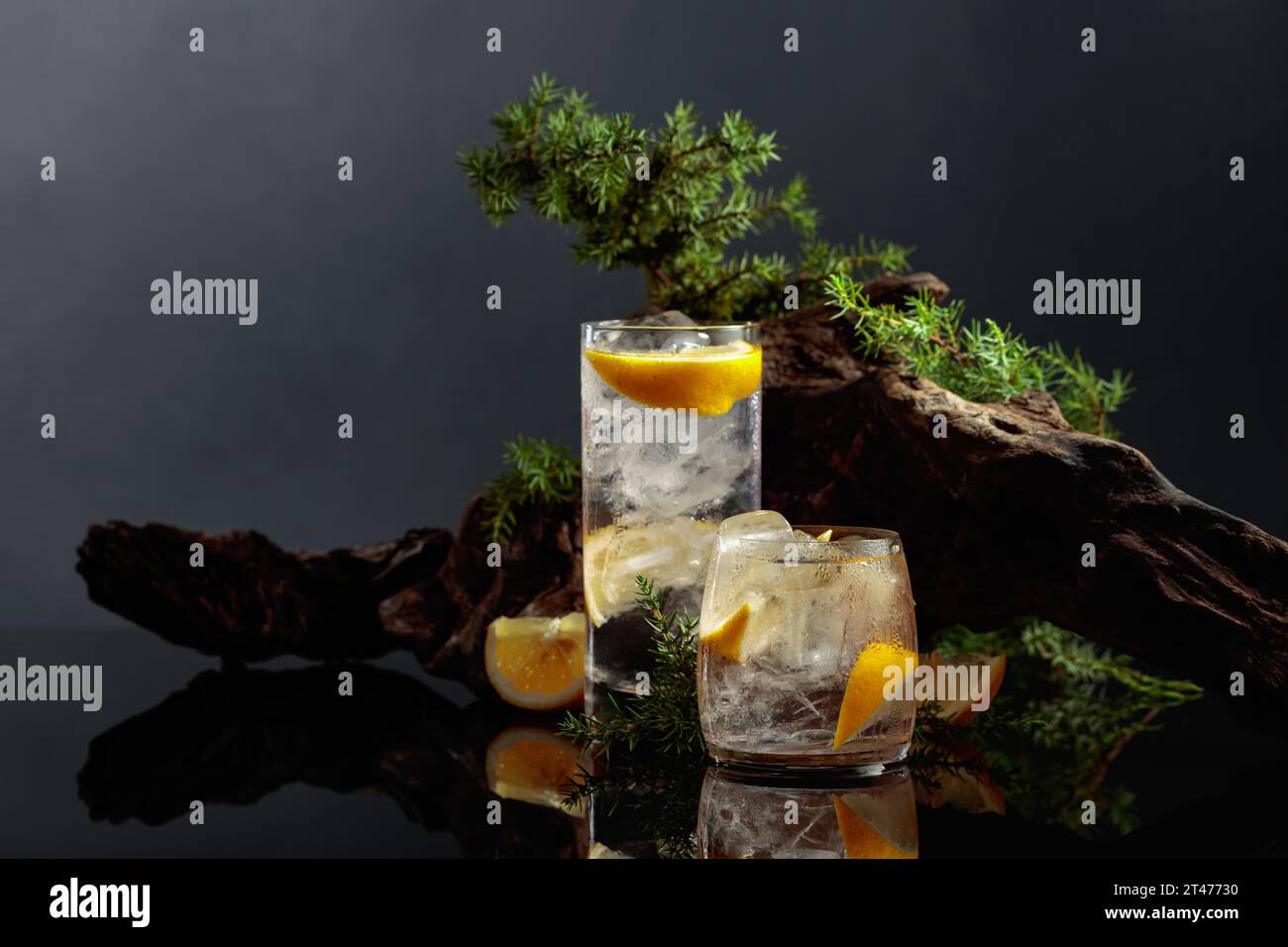 Cocktail gin-tonic with ice and lemon on a black reflective background ...