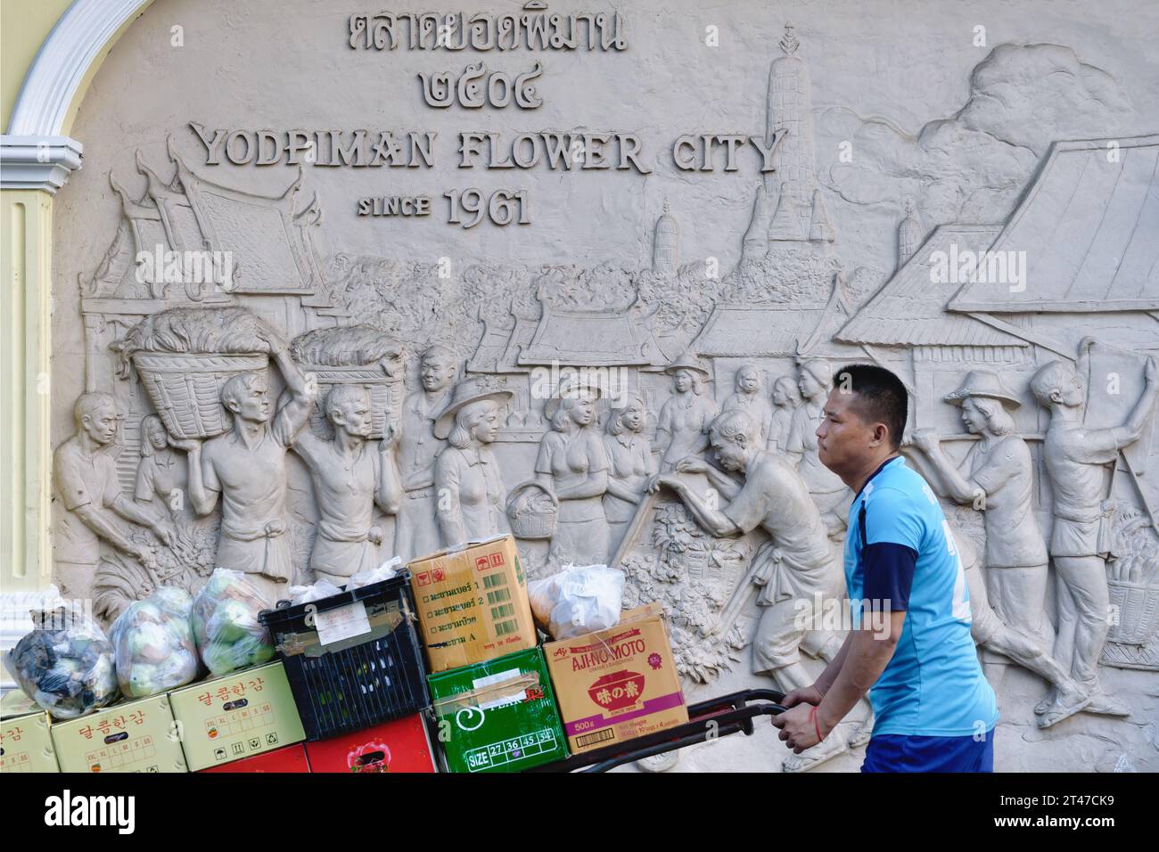 A man pushes a fully laden trolley past a frieze depicting a market ...