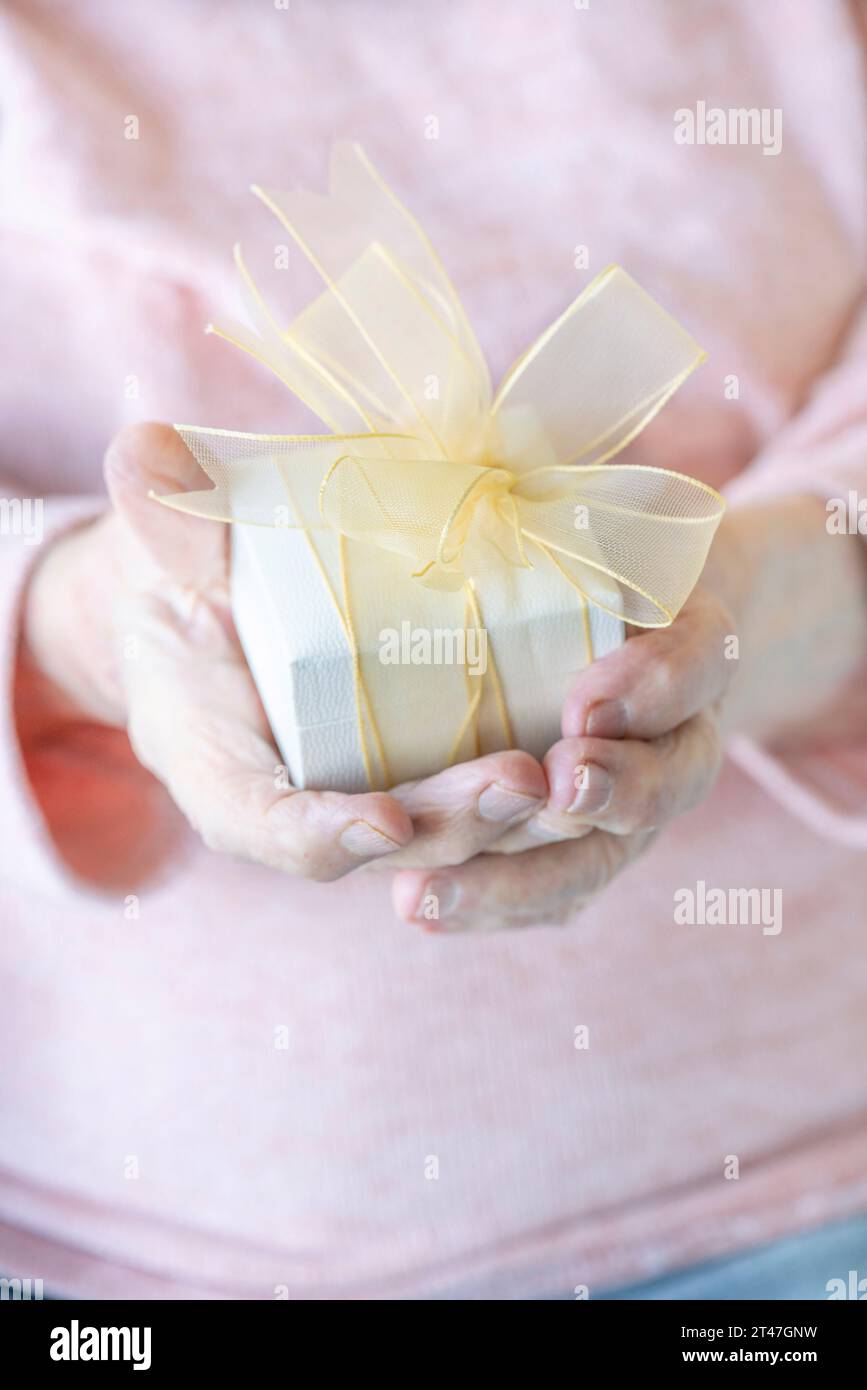 gift, closeup wrinkled hand of an old senior woman holding white gift ...