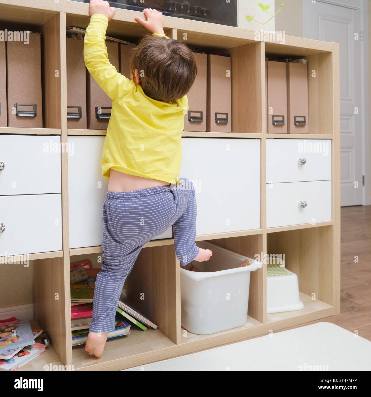 The little child is climbing up the cabinet, risking their safety. Kid ...