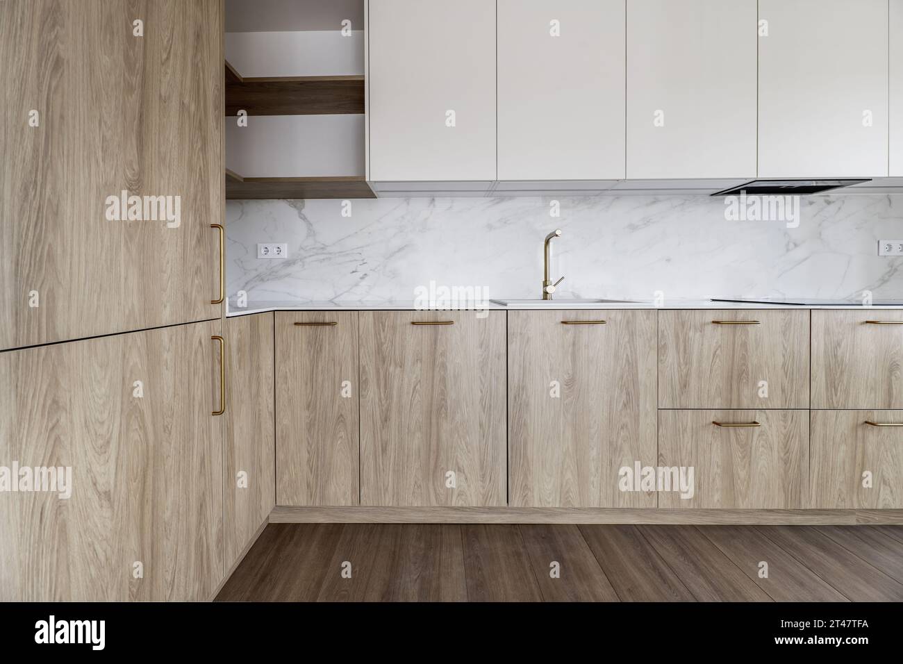 Corner of a modern kitchen with light wood furniture, golden metal ...