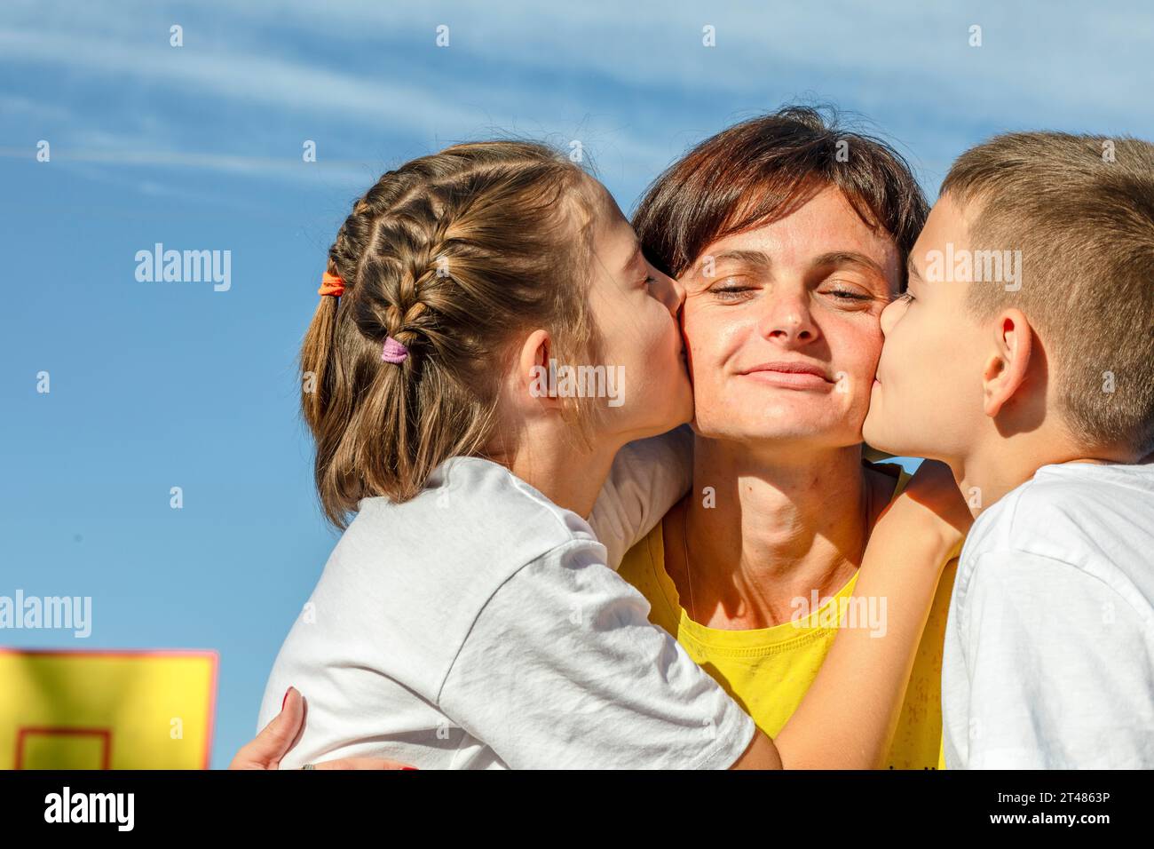 Outdoor hugs: Mother and teenage children cuddle gently in the sun on ...