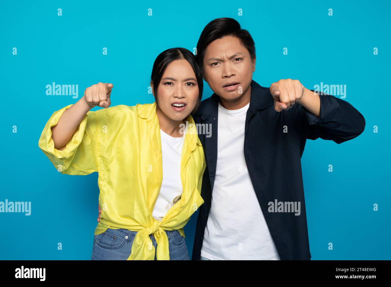 Confused sad serious asian couple in casual point fingers at camera ...