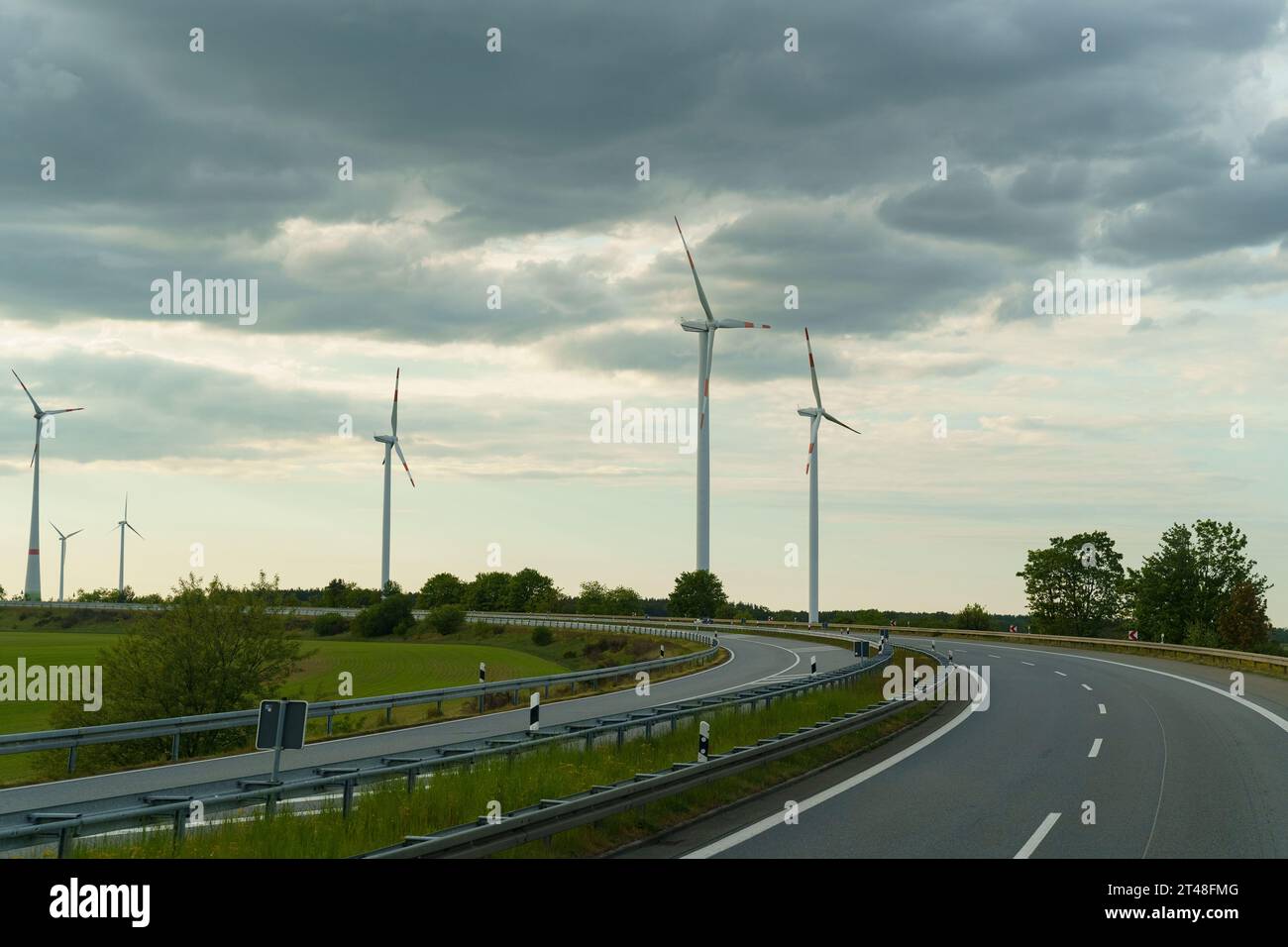 Wind turbines of a wind farm standing along the road. Renewable energy ...