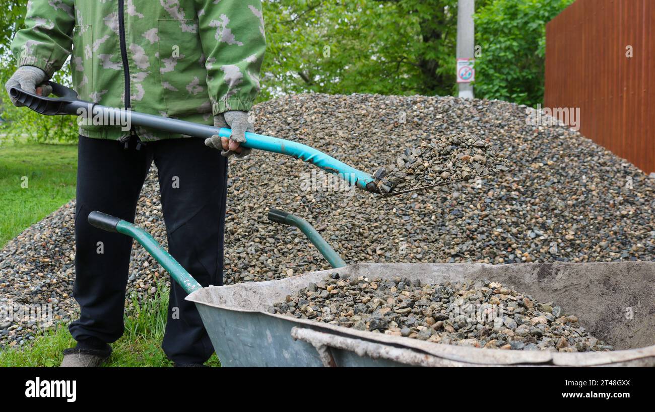 worker shoveling gray gravel from a pile on the ground into the metal ...