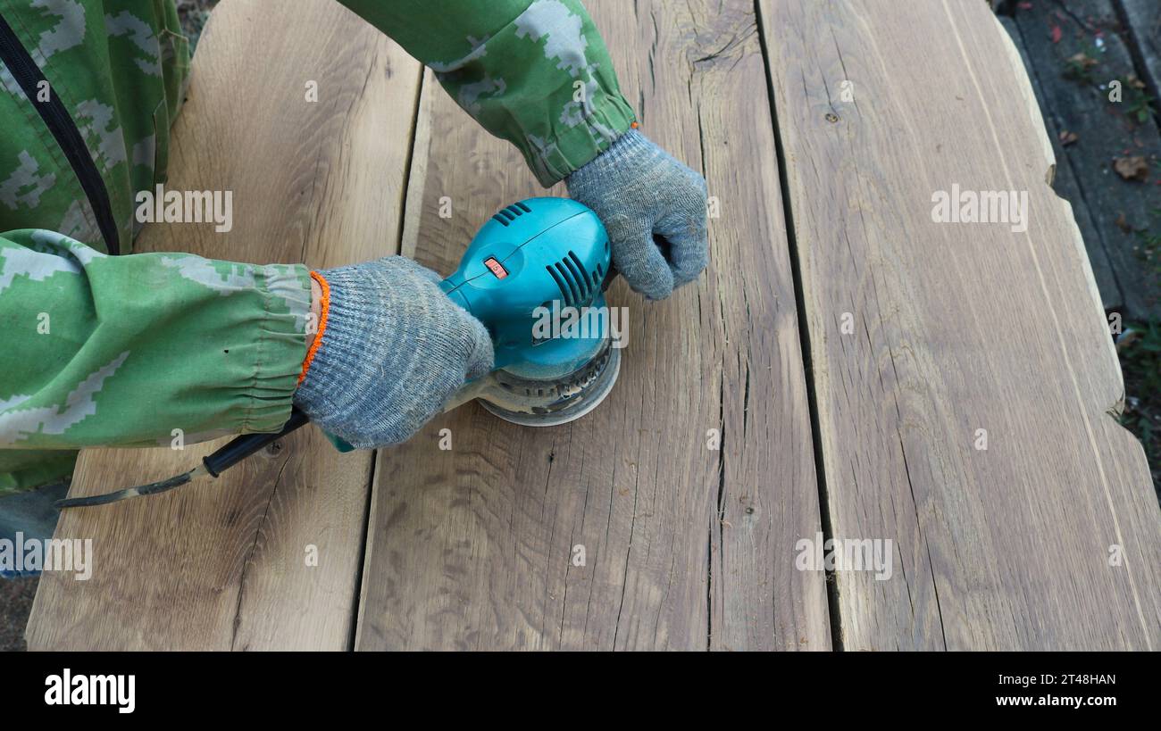 a carpenter sands the surface of solid oak boards holding the handle of ...