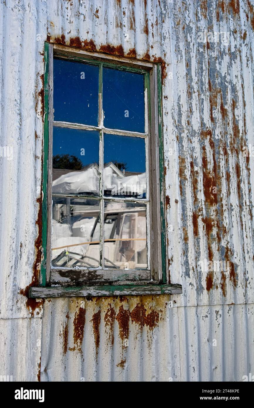 Distorted reflections of winterized boats in window of old rusty ...