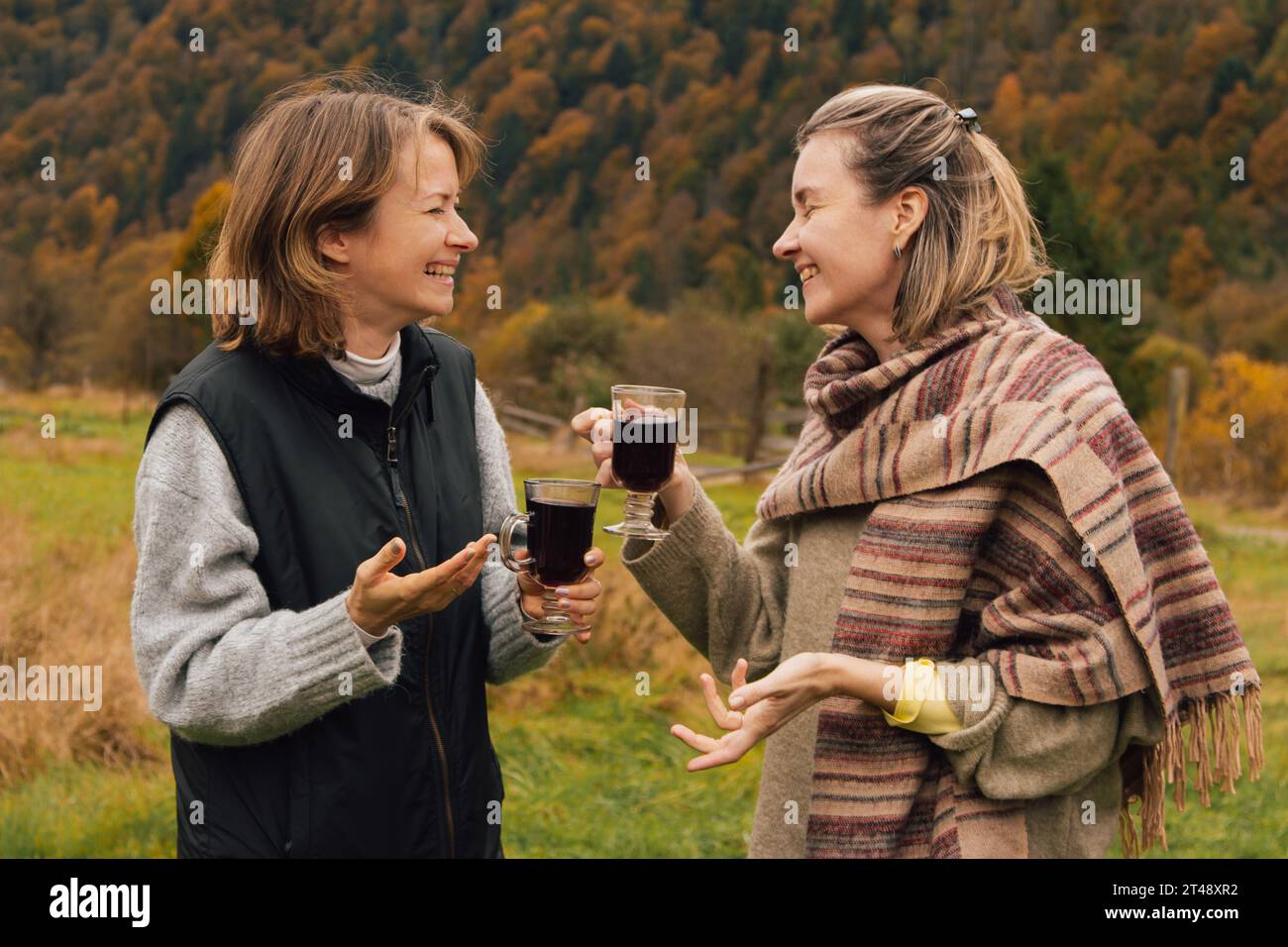 Two laughing women with mulled wine on autumn nature background. Two ...