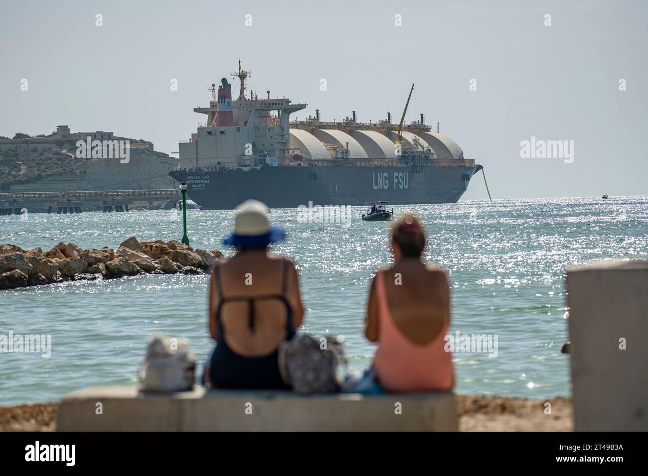 Two ladies in swimsuits enjoy the beach with the Armada LNG Mediterrana ...